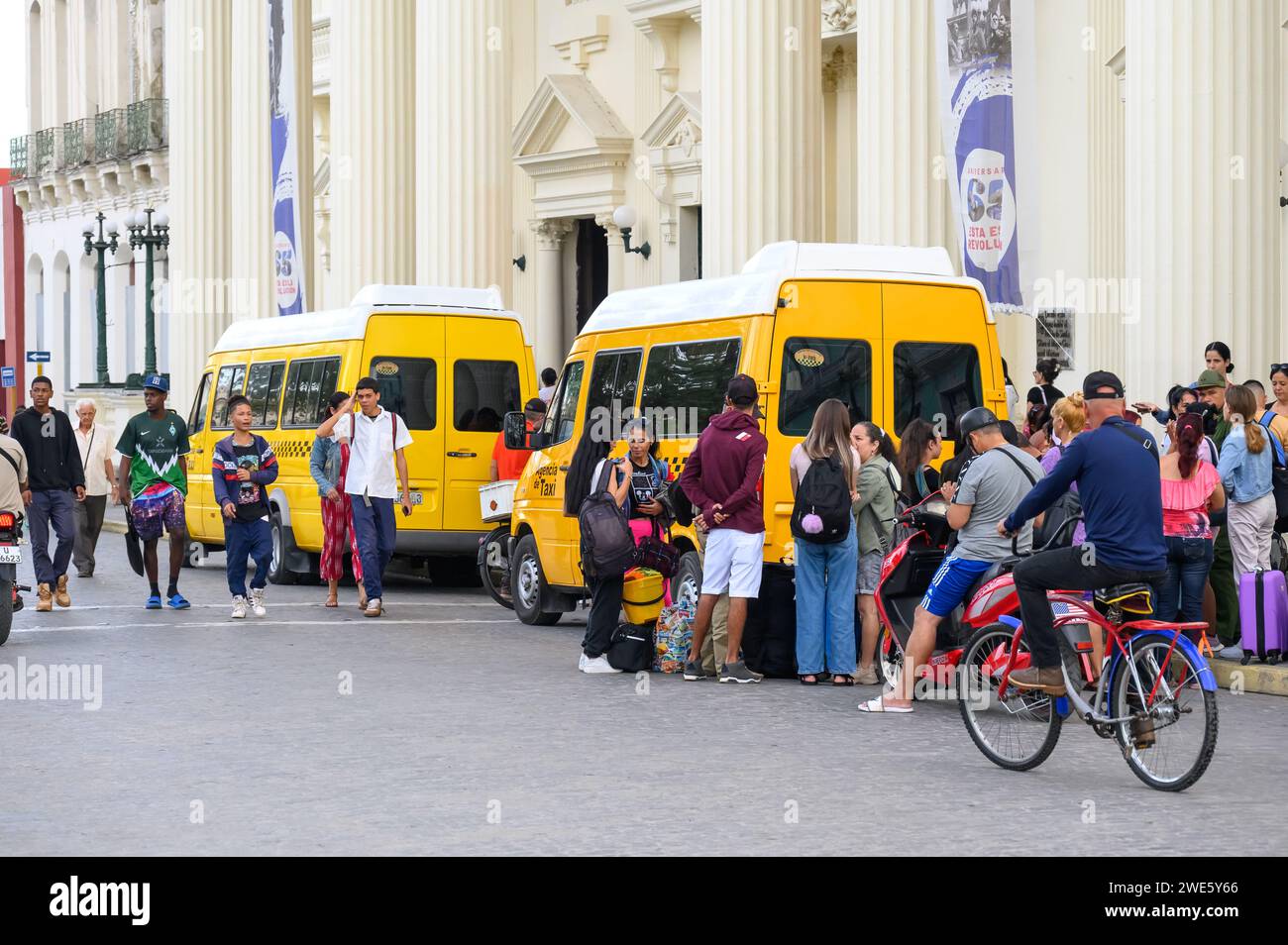 A large group of Cuban people by two van taxis in the Jose Marti Public ...