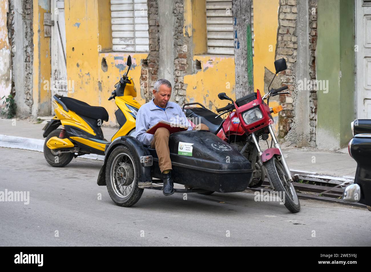 A Cuban man reads a document in a sidecar motorcyle. He is waiting for ...