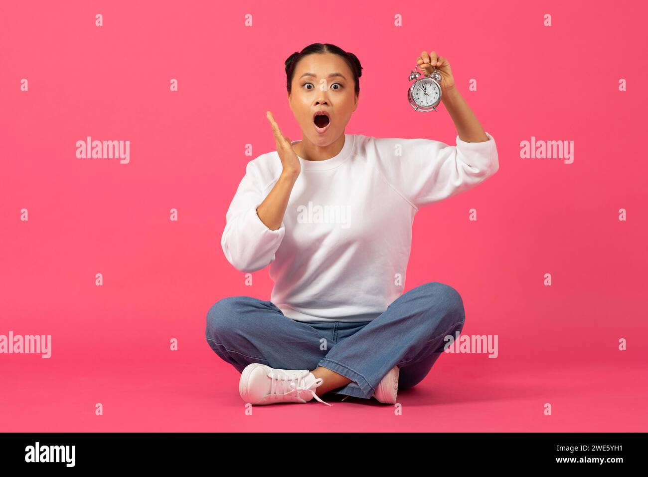 Shocked young asian woman sitting on floor and holding alarm clock ...