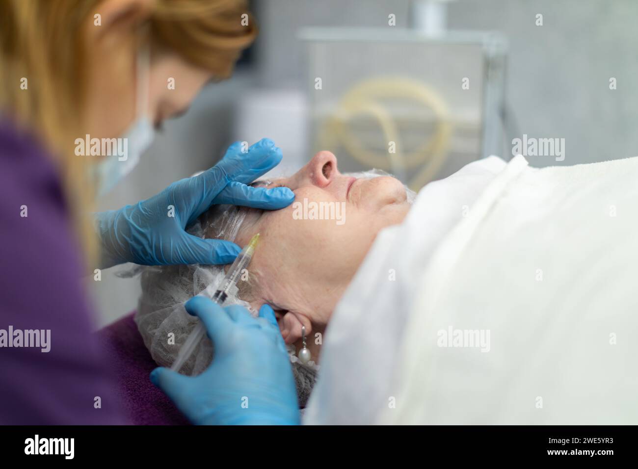 A nurse inserts a needle into the facial skin of a clinic patient Stock ...