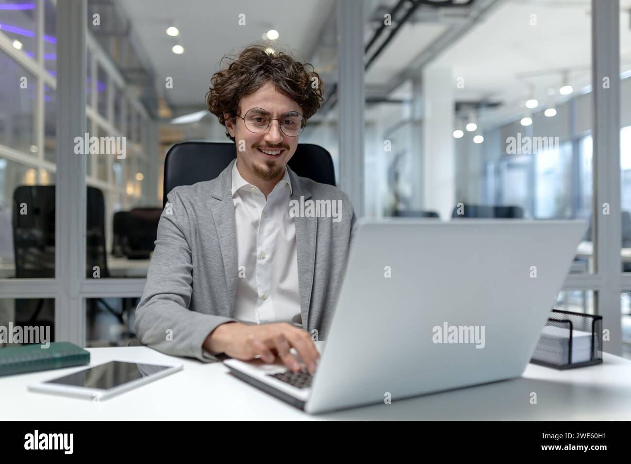 Young, professional male office worker with curly hair typing on a ...