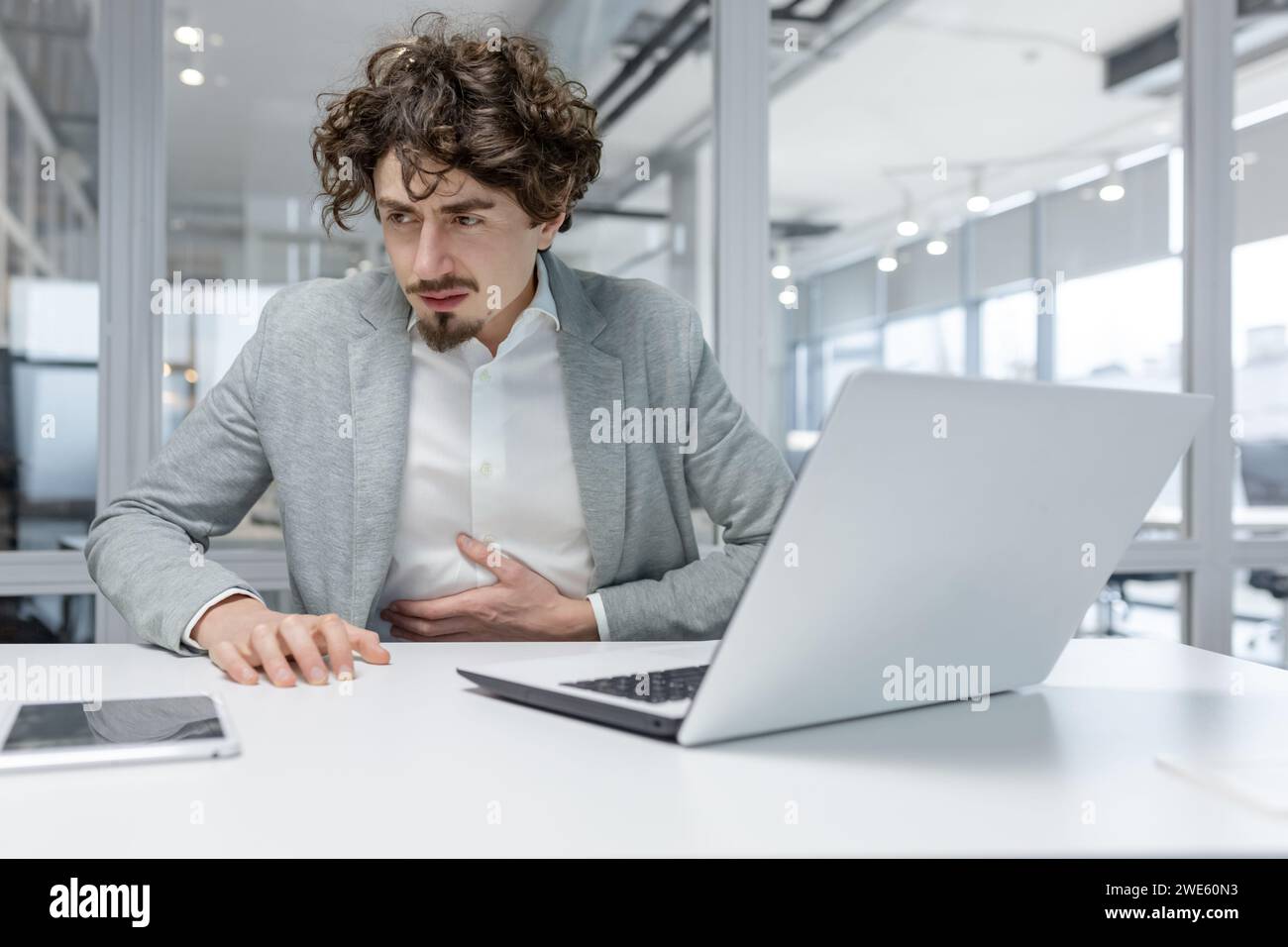 Adult businessman feeling unwell at his workplace in a modern office ...