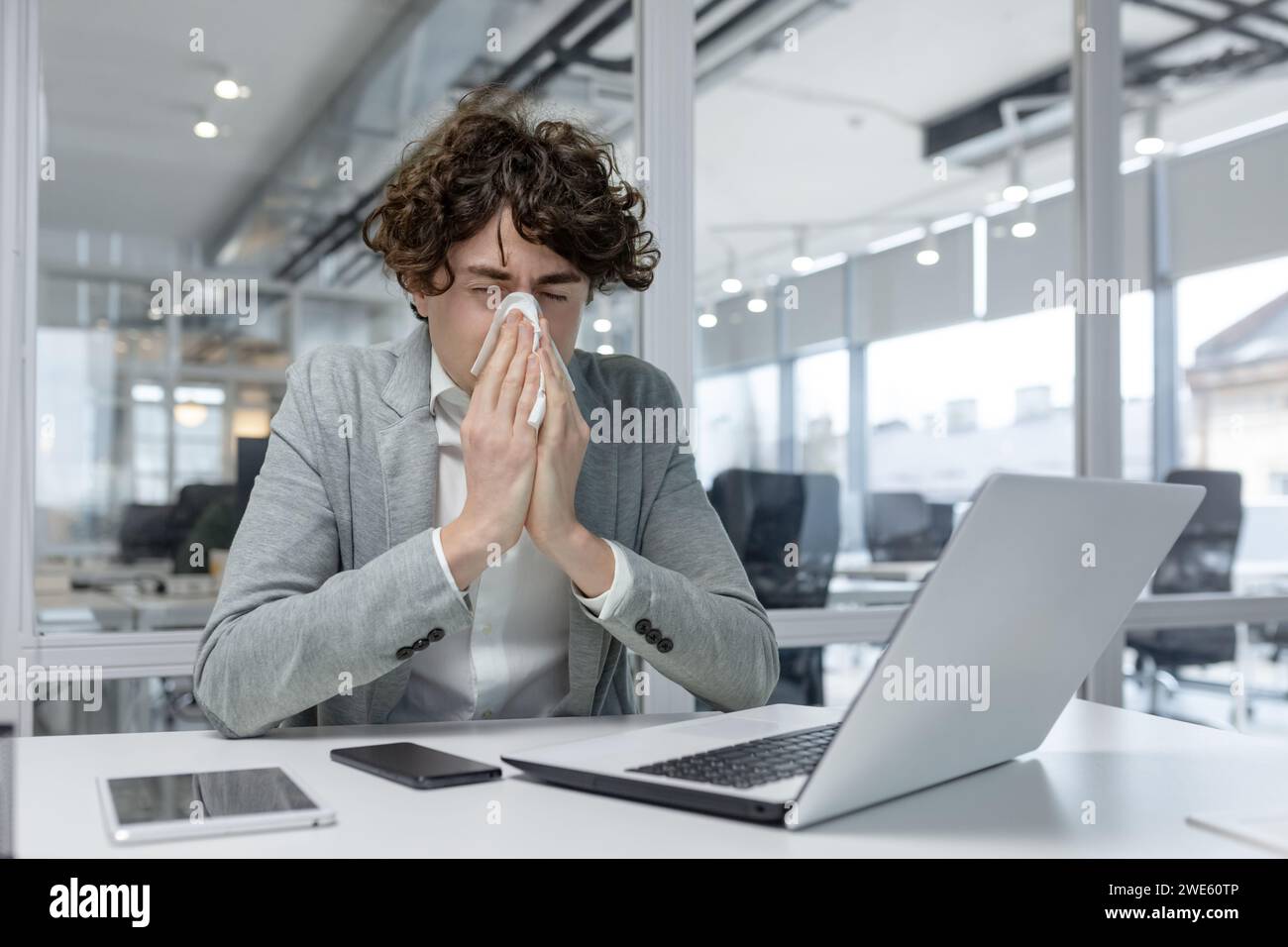 Exhausted young adult businessman caught a cold, working with a laptop ...