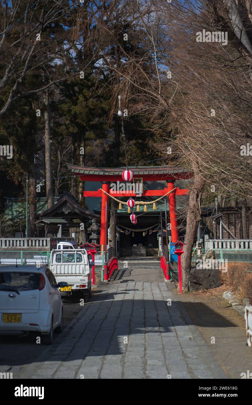 A vibrant red torii gate stands before a row of parked cars Stock Photo ...