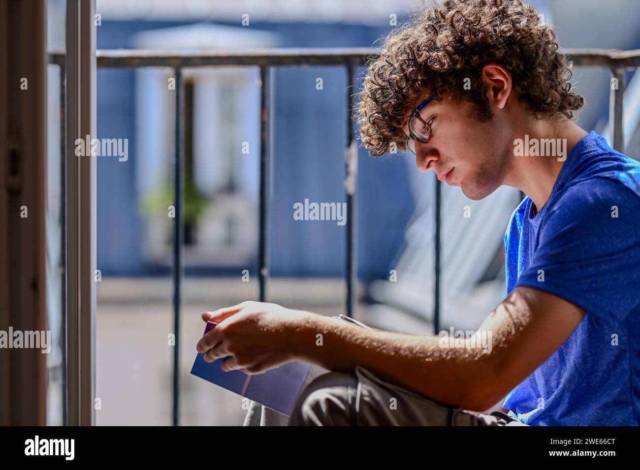 Nice shot of a young Caucasian man reading a book. He is sitting on an ...
