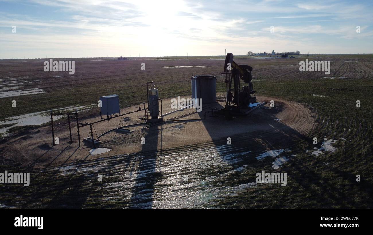 A male individual stands before an oil well, situated along a dusty ...