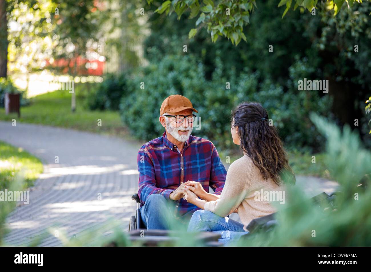Smiling retired senior man in wheelchair holding hands with social ...