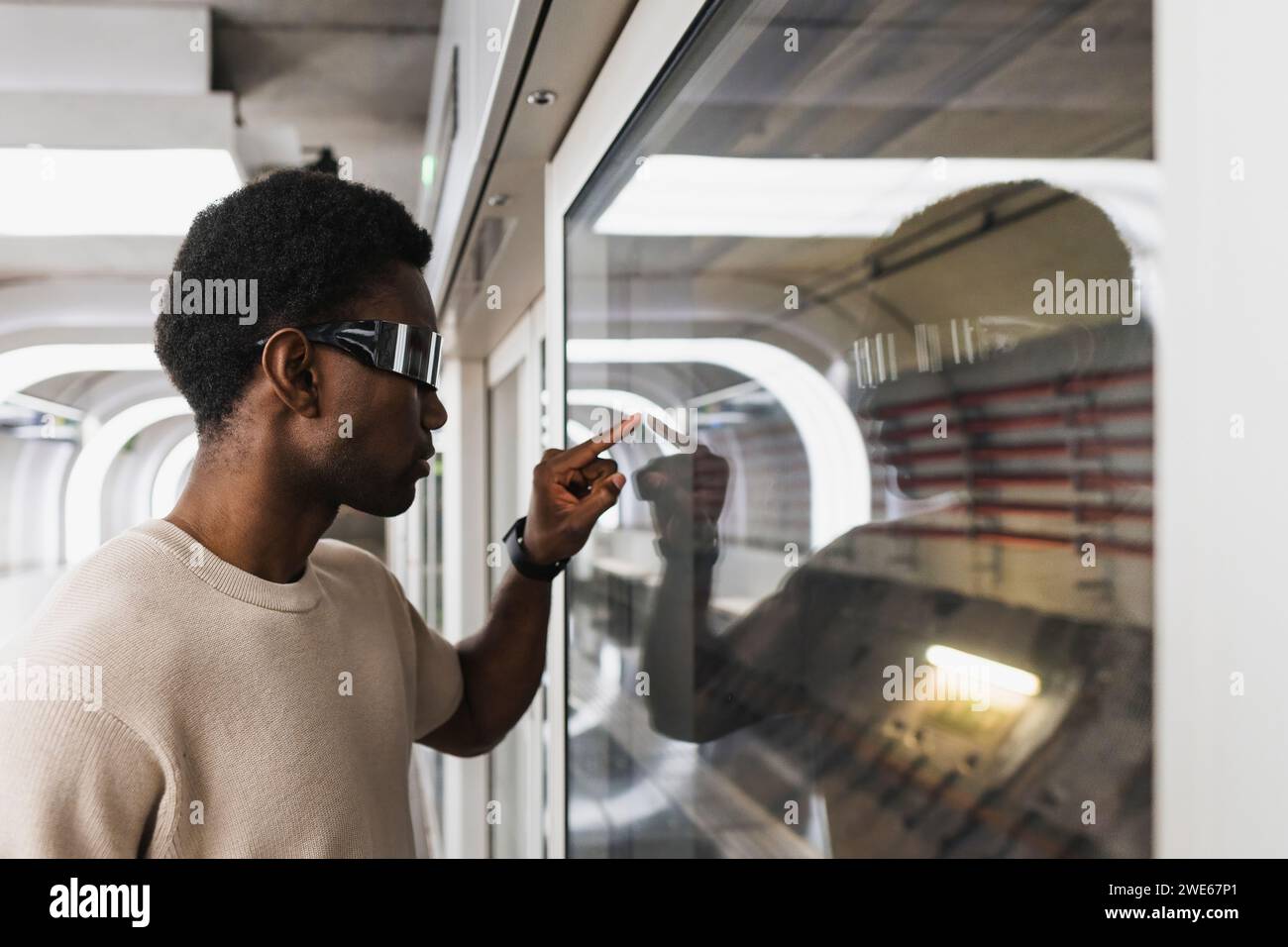 Young man with cyber glasses touching glass pane with his forefinger ...