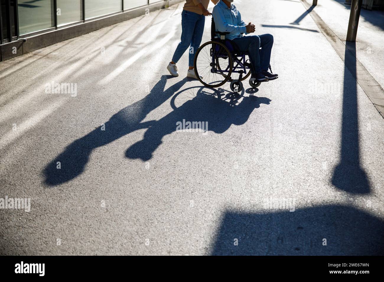 Caregiver pushing man in wheelchair on footpath with shadow Stock Photo ...