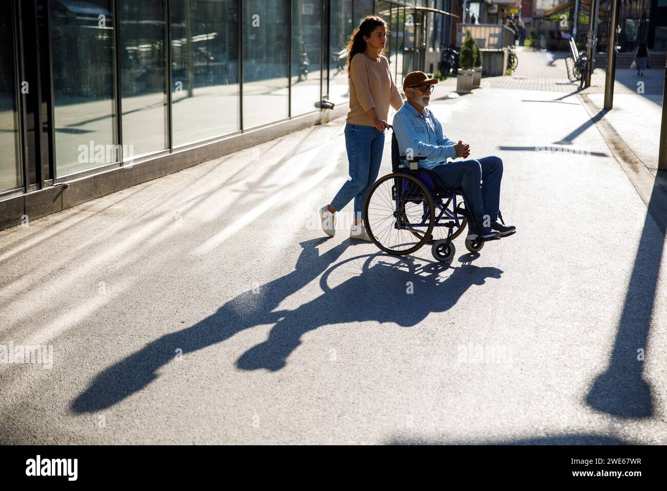Volunteer pushing man in wheelchair on footpath with shadow Stock Photo ...