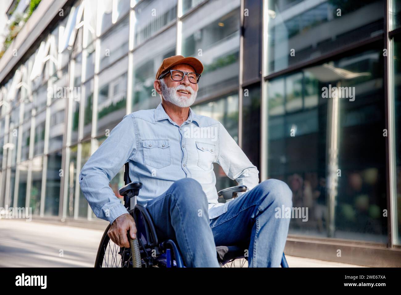 Smiling senior man sitting in wheelchair on footpath Stock Photo - Alamy