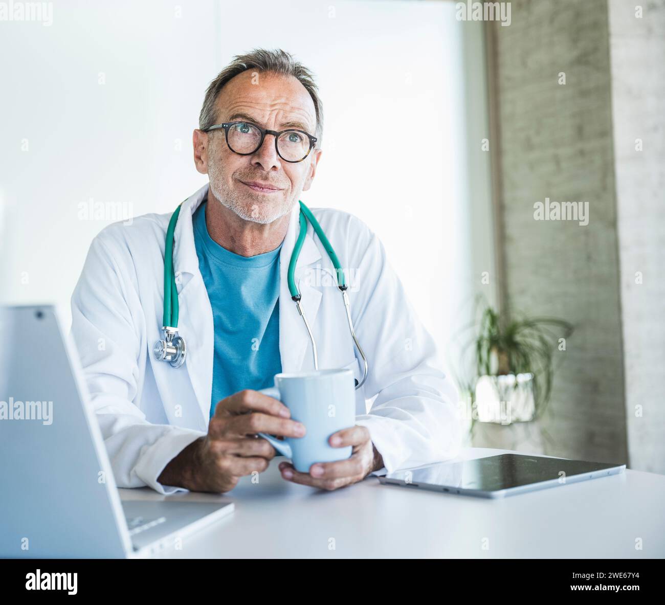 Thoughtful senior doctor sitting with coffee cup at desk Stock Photo ...