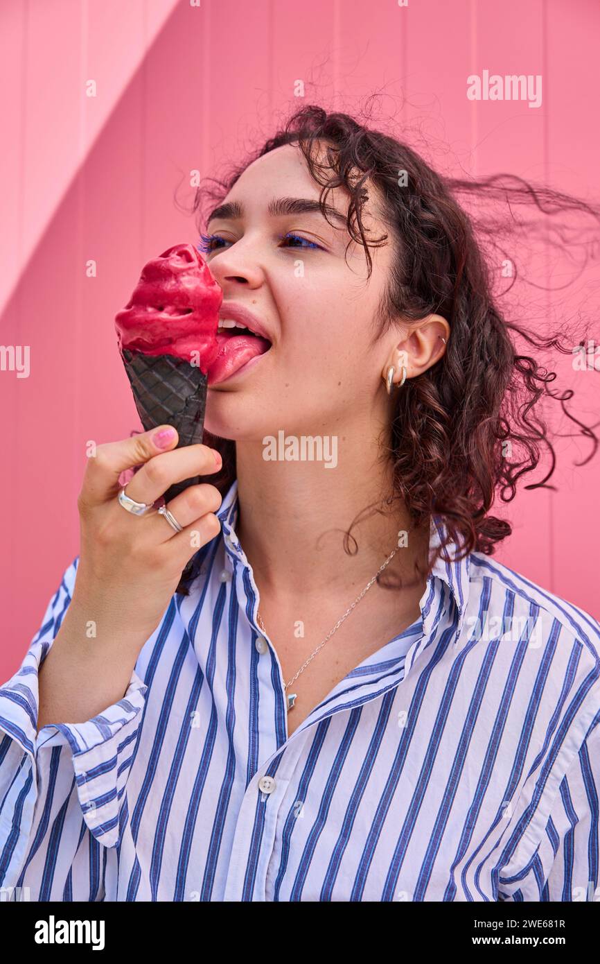 Happy woman licking ice cream in front of pink wall Stock Photo - Alamy
