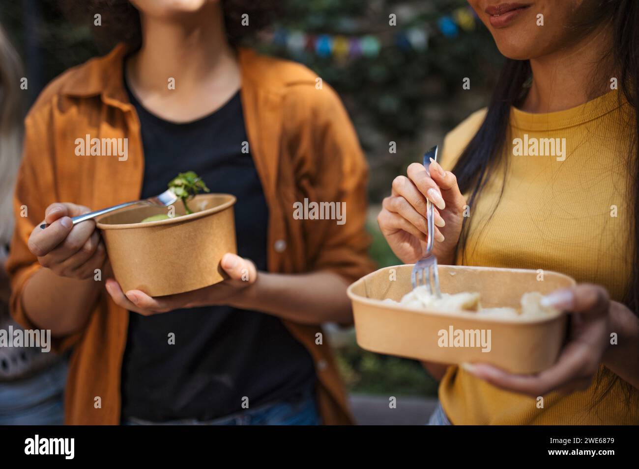 Happy friends eating together in garden from disposable containers ...