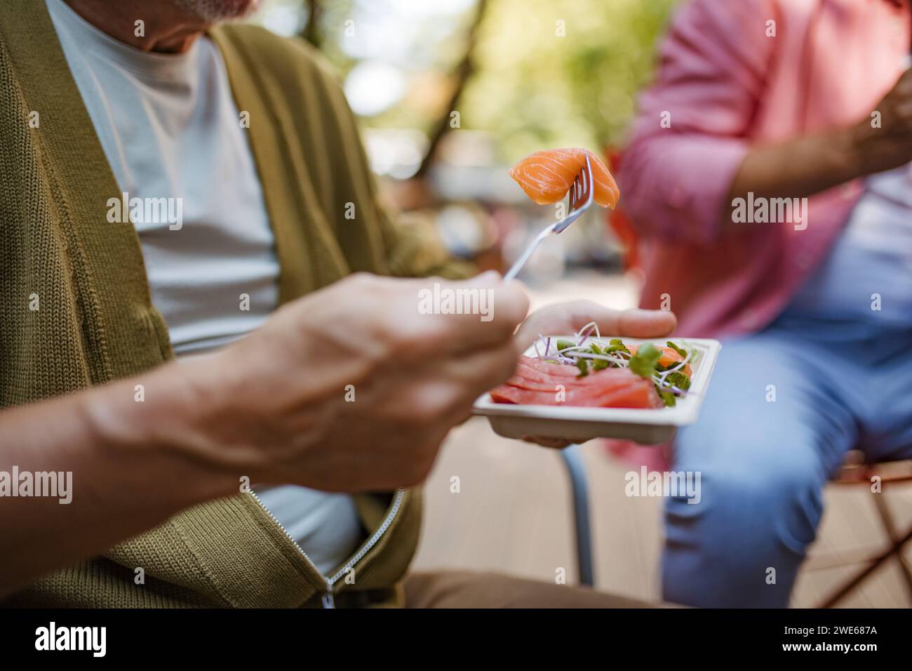 Happy friends eating together in garden from disposable containers ...