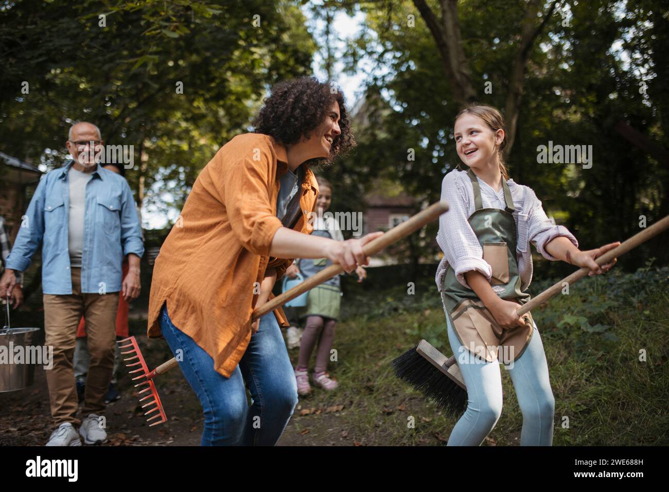 Woman and girl pretending to ride on broom sticks at community garden ...