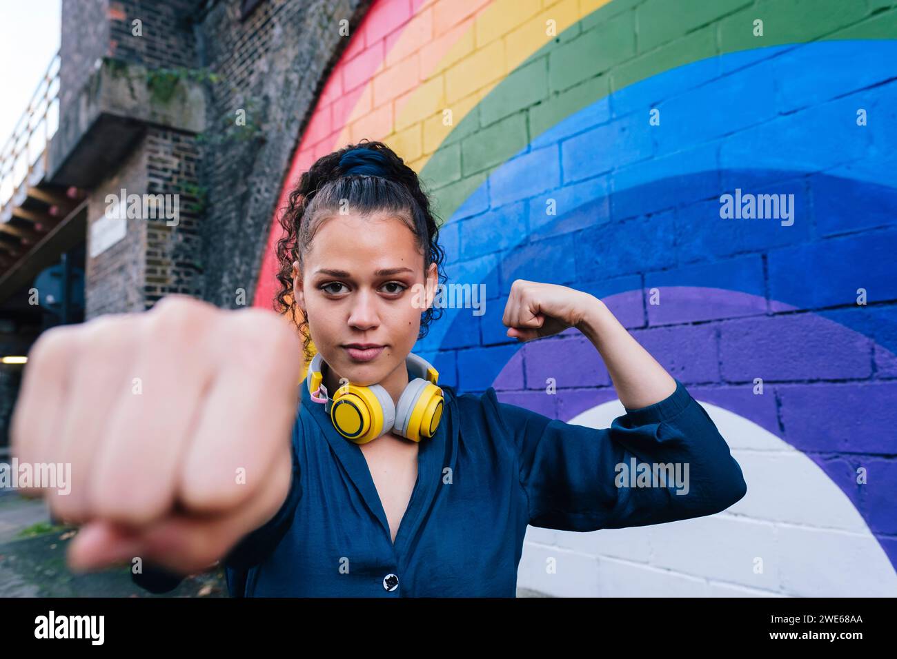 Young woman punching with fist and flexing muscle in front of wall ...