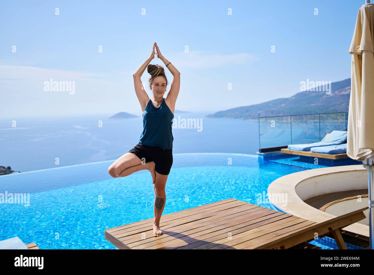 Woman doing tree pose on deck chair near swimming pool Stock Photo - Alamy