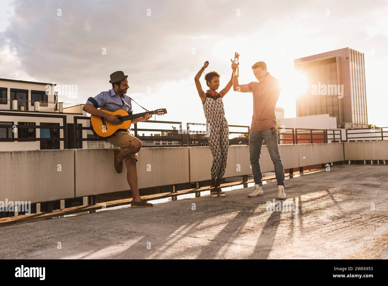 Happy man playing guitar with friends dancing on rooftop Stock Photo ...