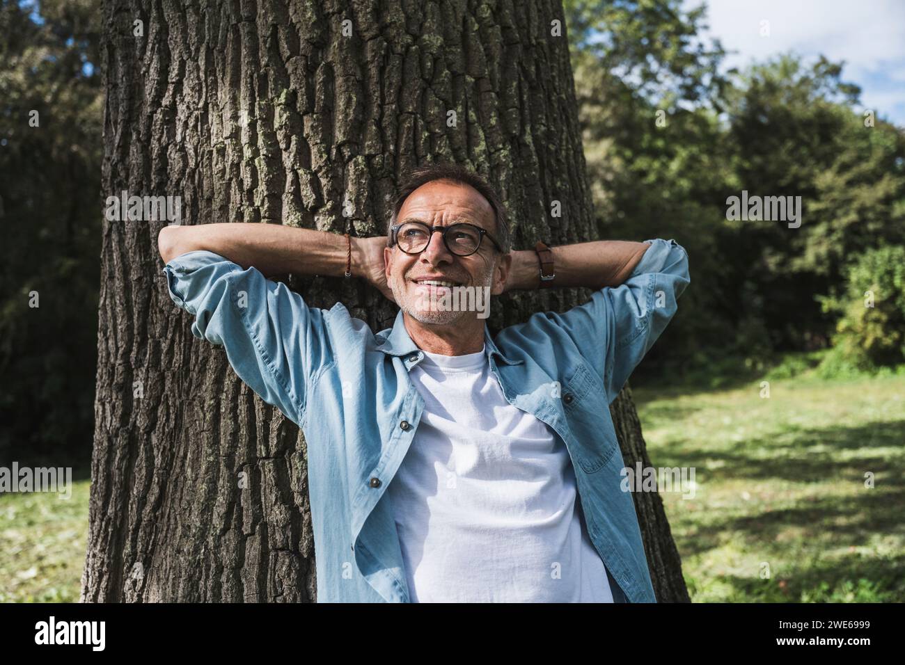 Contemplative man with hands behind head in front of tree at park Stock ...