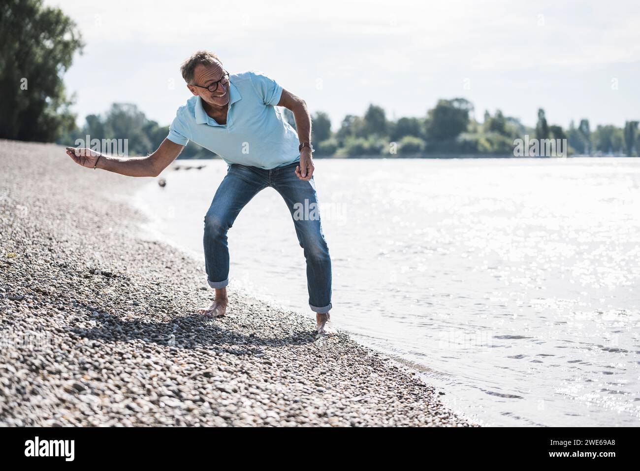 Smiling senior man throwing pebble in sea at beach Stock Photo - Alamy