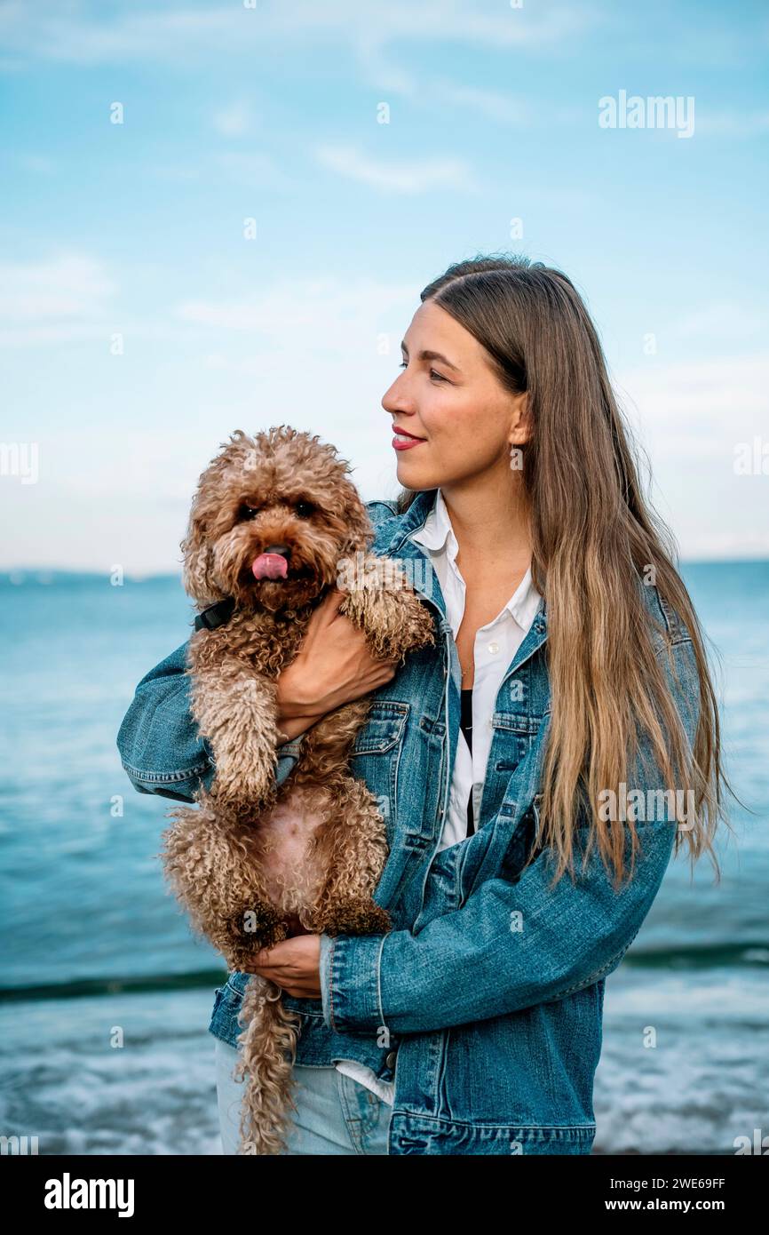 Smiling young woman with poodle dog standing at beach Stock Photo - Alamy