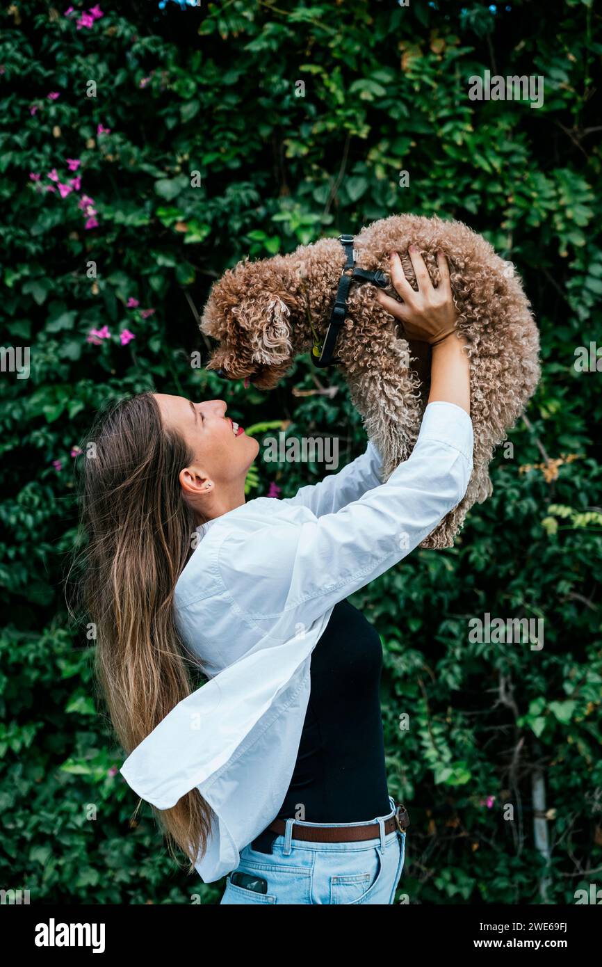 Happy young woman holding poodle dog aloft in front of plants Stock ...