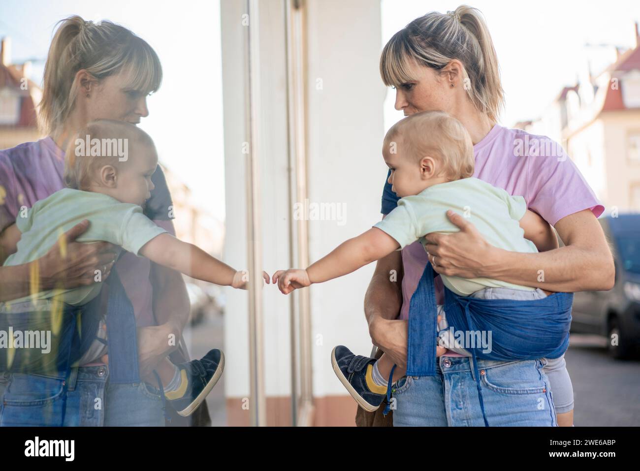 Mother carrying son touching store window at street Stock Photo - Alamy