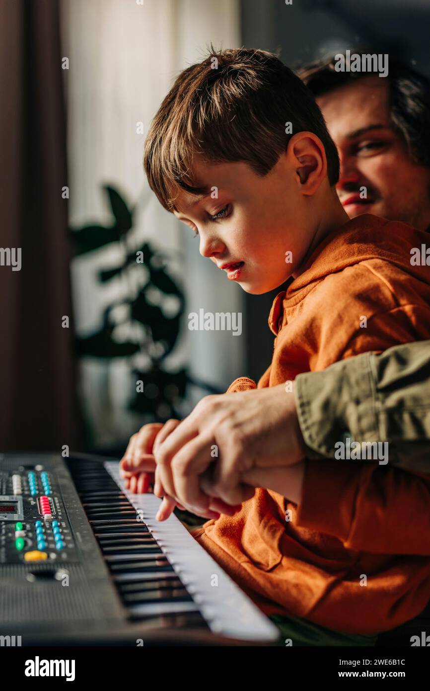 Father holding hands and teaching electric piano to son at home Stock ...
