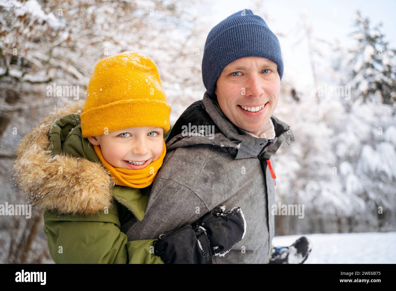 Happy father giving piggyback ride to son in winter forest Stock Photo ...