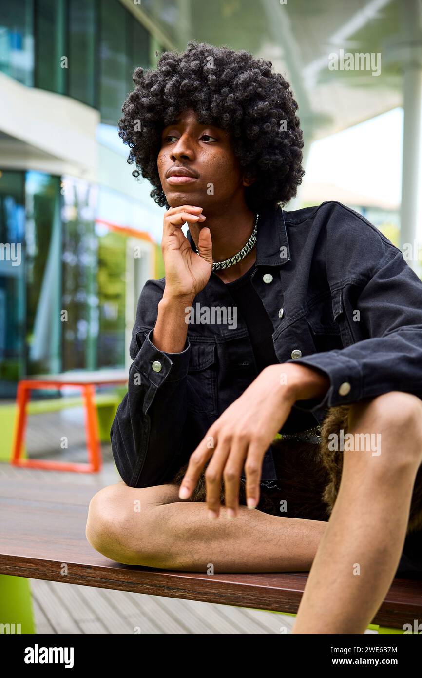 Non-binary person with curly hair sitting on bench Stock Photo - Alamy