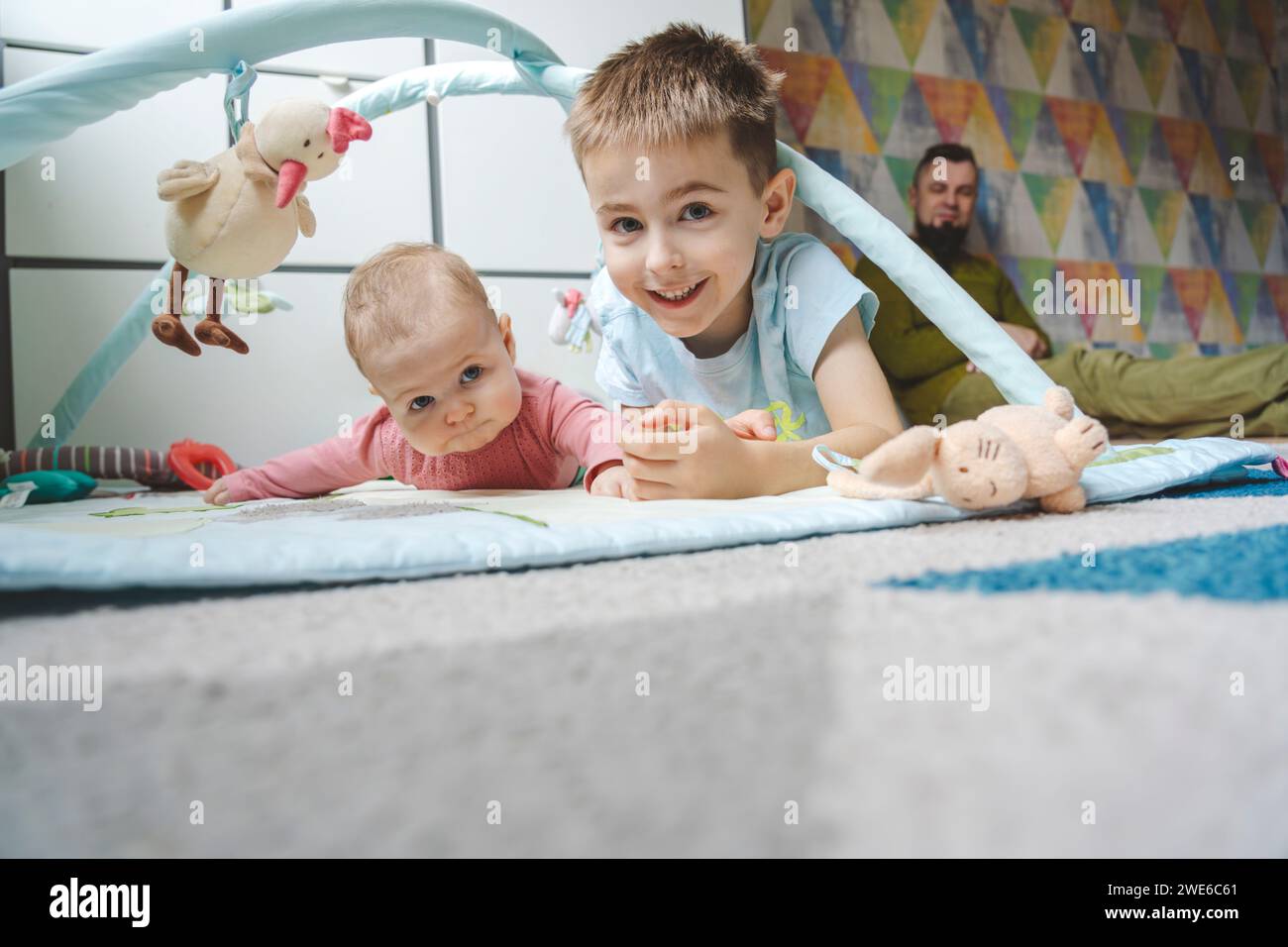 Smiling brother with baby sister lying on mat at home Stock Photo - Alamy