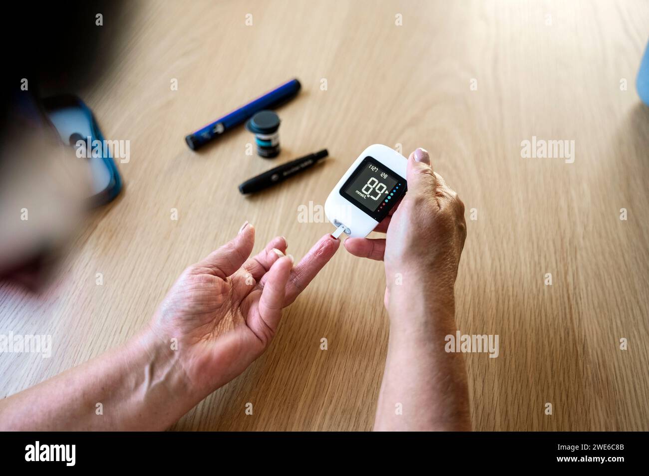 Hands of senior woman doing blood sugar test with glucometer at table ...