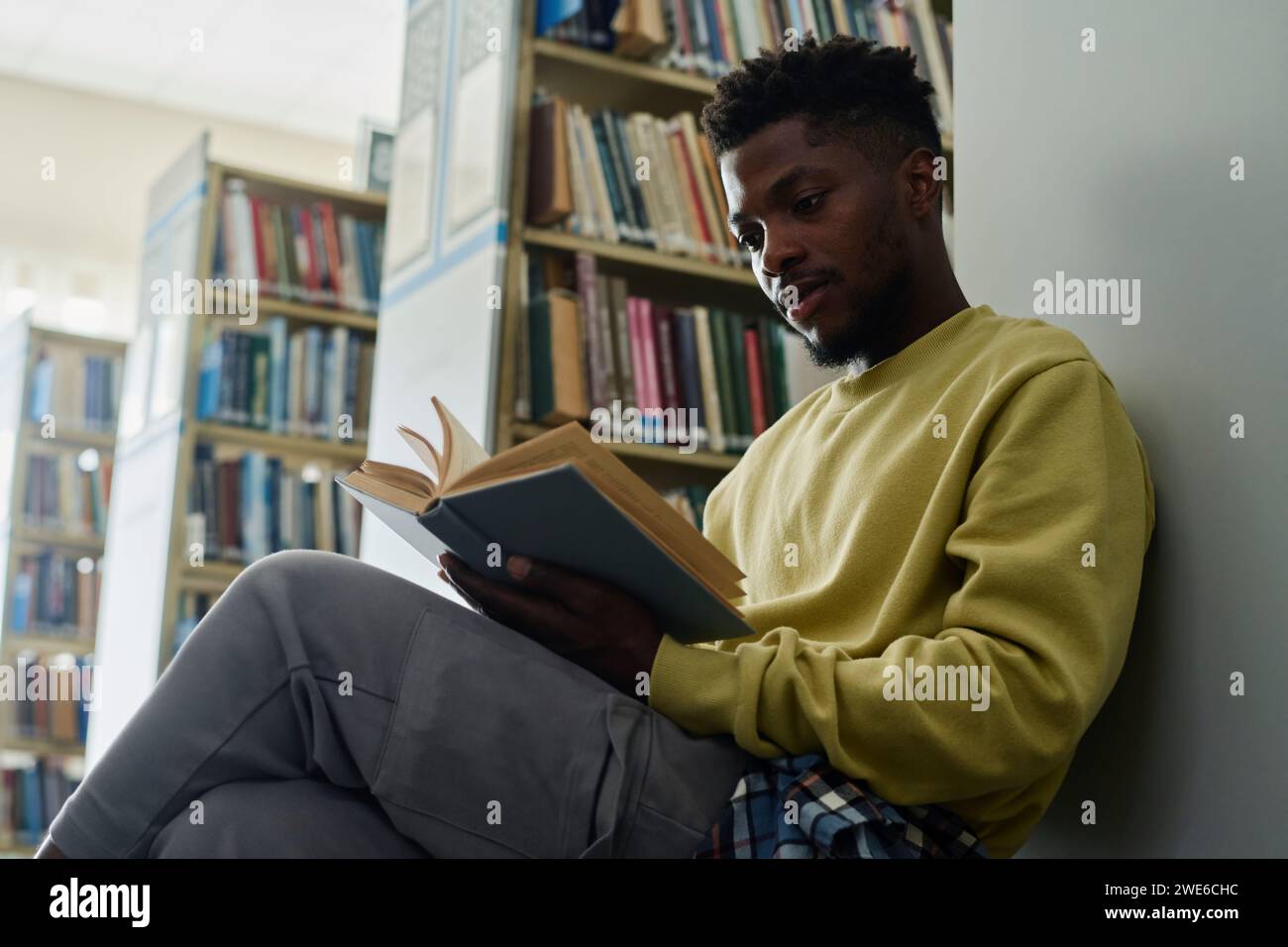 Student leaning on shelf and reading book in library Stock Photo - Alamy