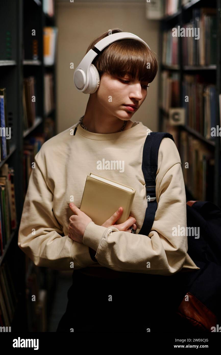 Student wearing wireless headphones and holding book in library Stock ...
