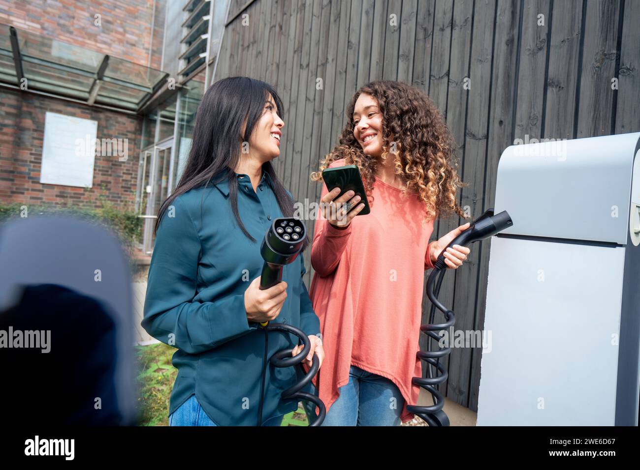 Happy friends with electric plugs at charging station Stock Photo - Alamy