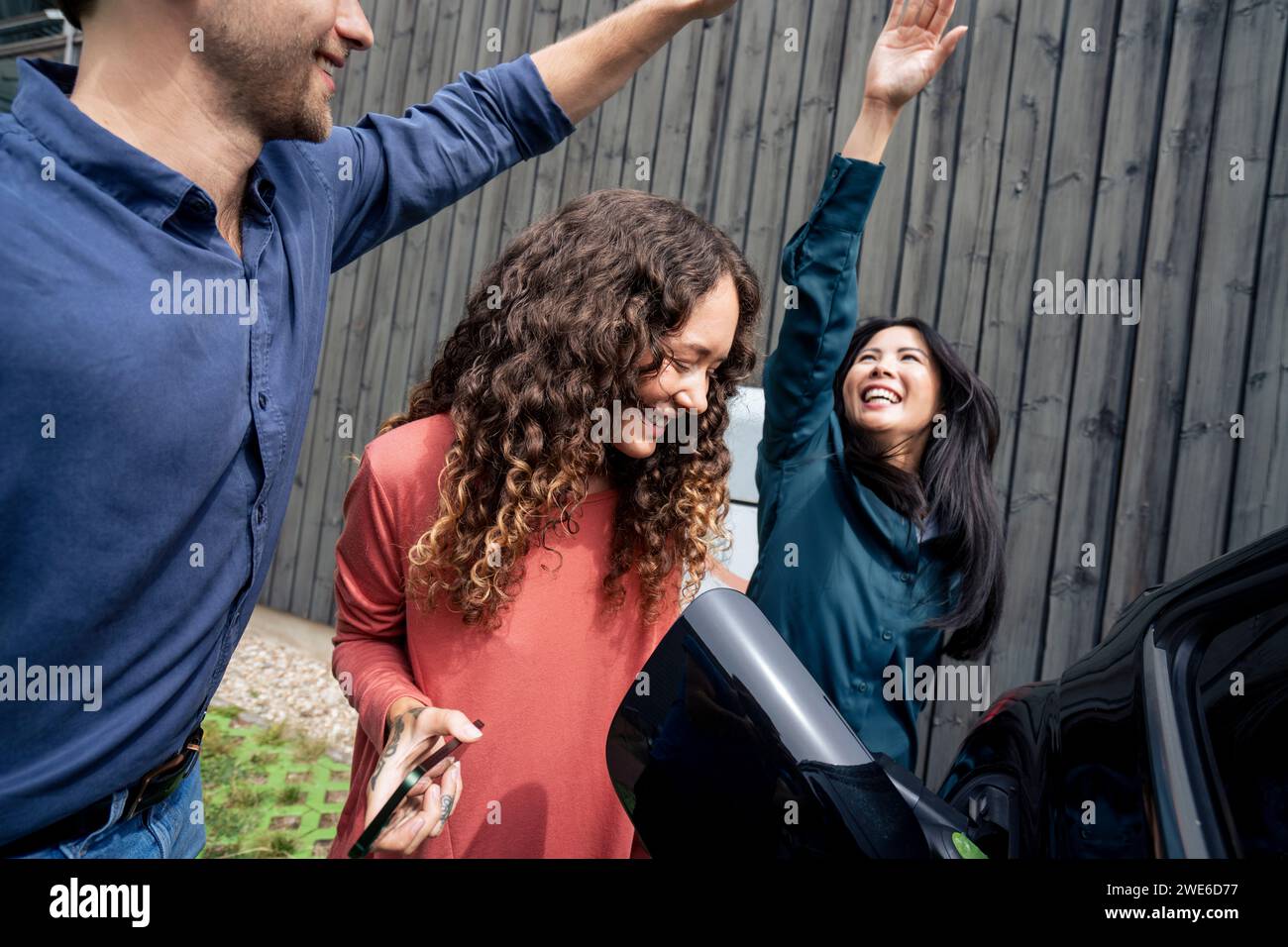 Happy friends standing by electric car getting charged Stock Photo - Alamy