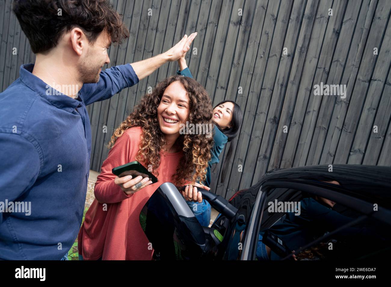 Man and woman doing high-five by friend charging electric car Stock ...