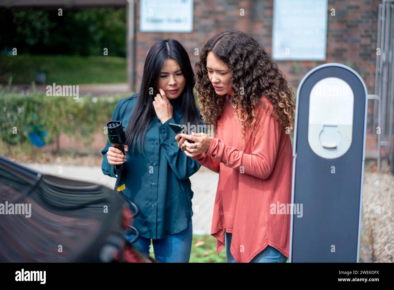 Woman holding electric plug and sharing mobile phone with friend at ...