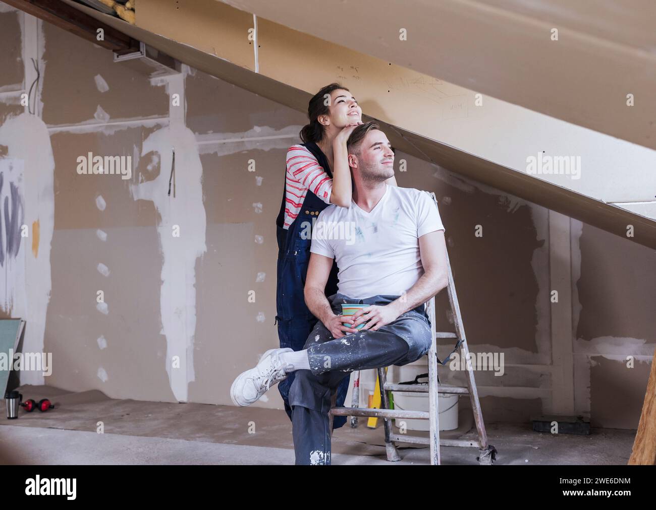 Smiling man sitting on ladder with woman standing at home Stock Photo ...