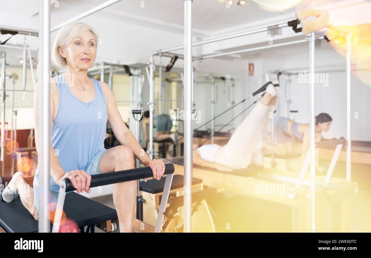 Mature woman practicing pilates stretching exercises on reformer at gym ...