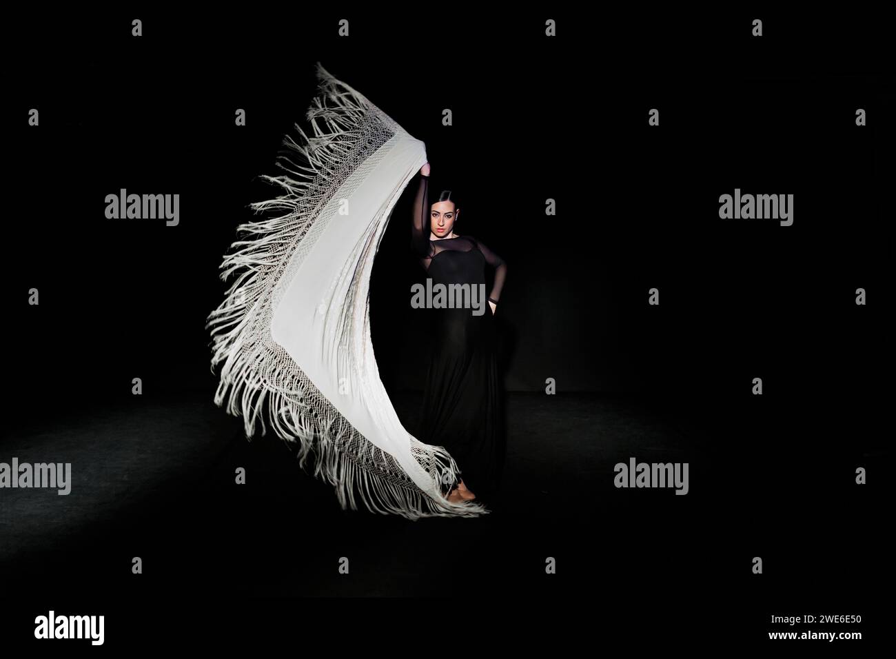Graceful woman performing flamenco dance with shawl against black ...