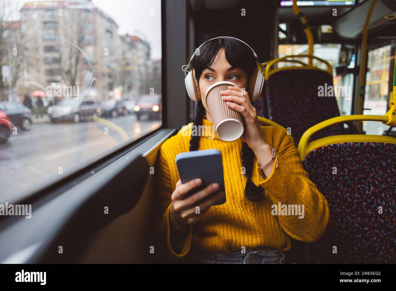 Woman wearing wireless headphones and drinking coffee in bus Stock ...