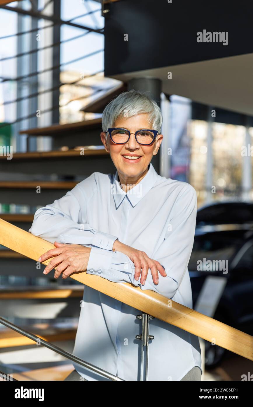 Smiling businesswoman wearing eyeglasses and leaning on railing at ...