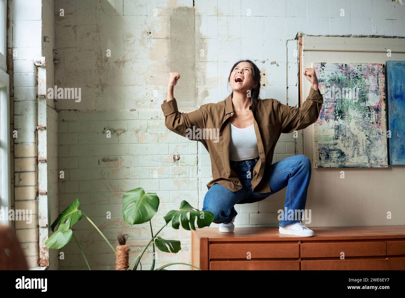 Excited painter shouting in joy squatting on cabinet by paintings at ...