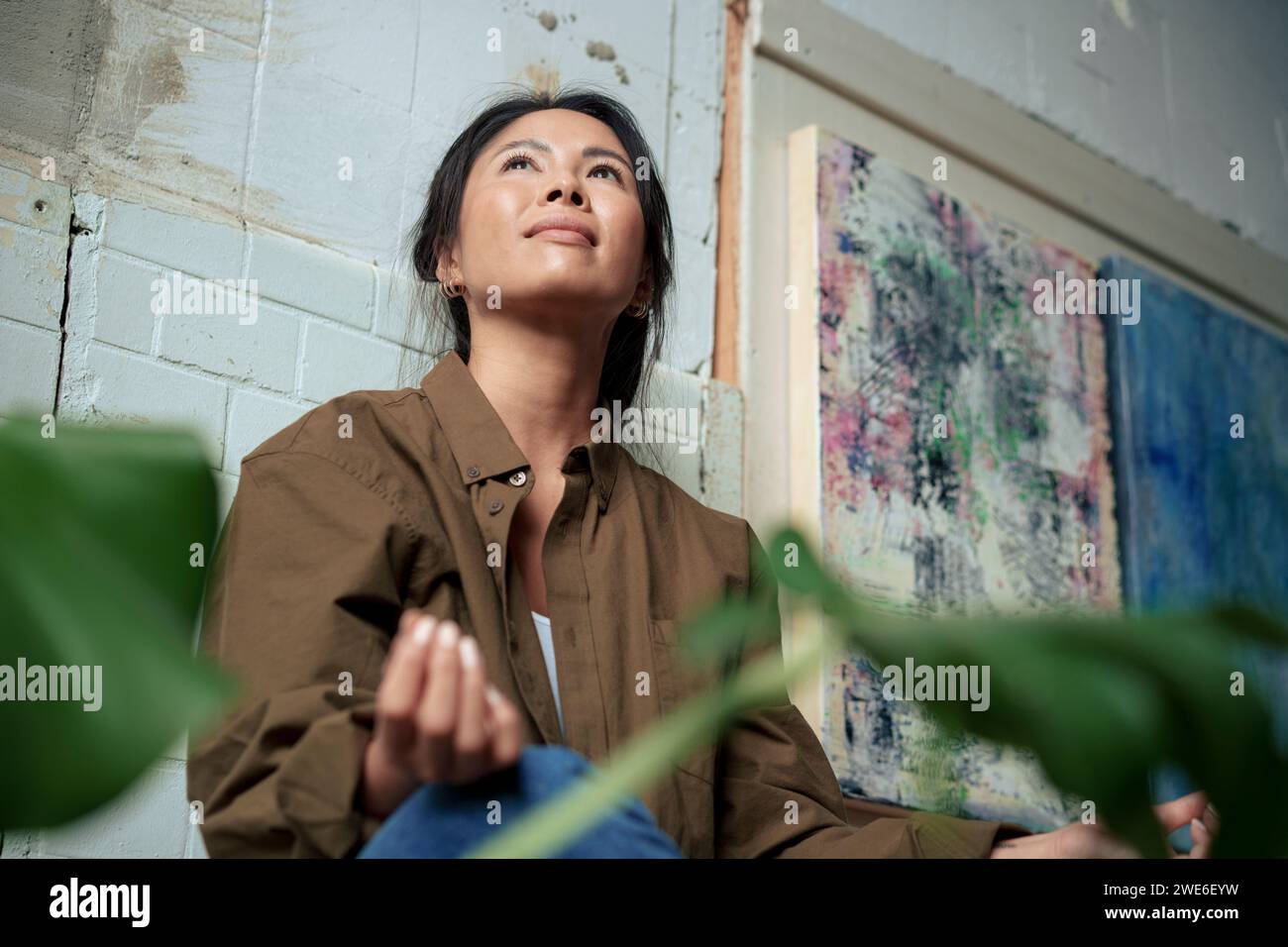Smiling painter sitting cross-legged by paintings at art studio Stock ...