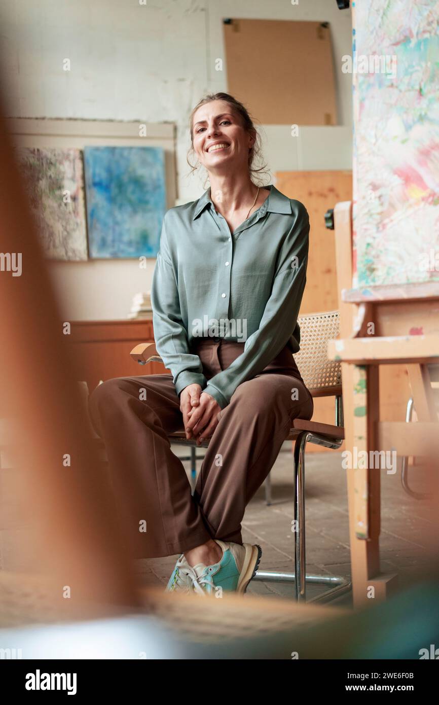 Painter sitting cross-legged on chair in art studio Stock Photo - Alamy