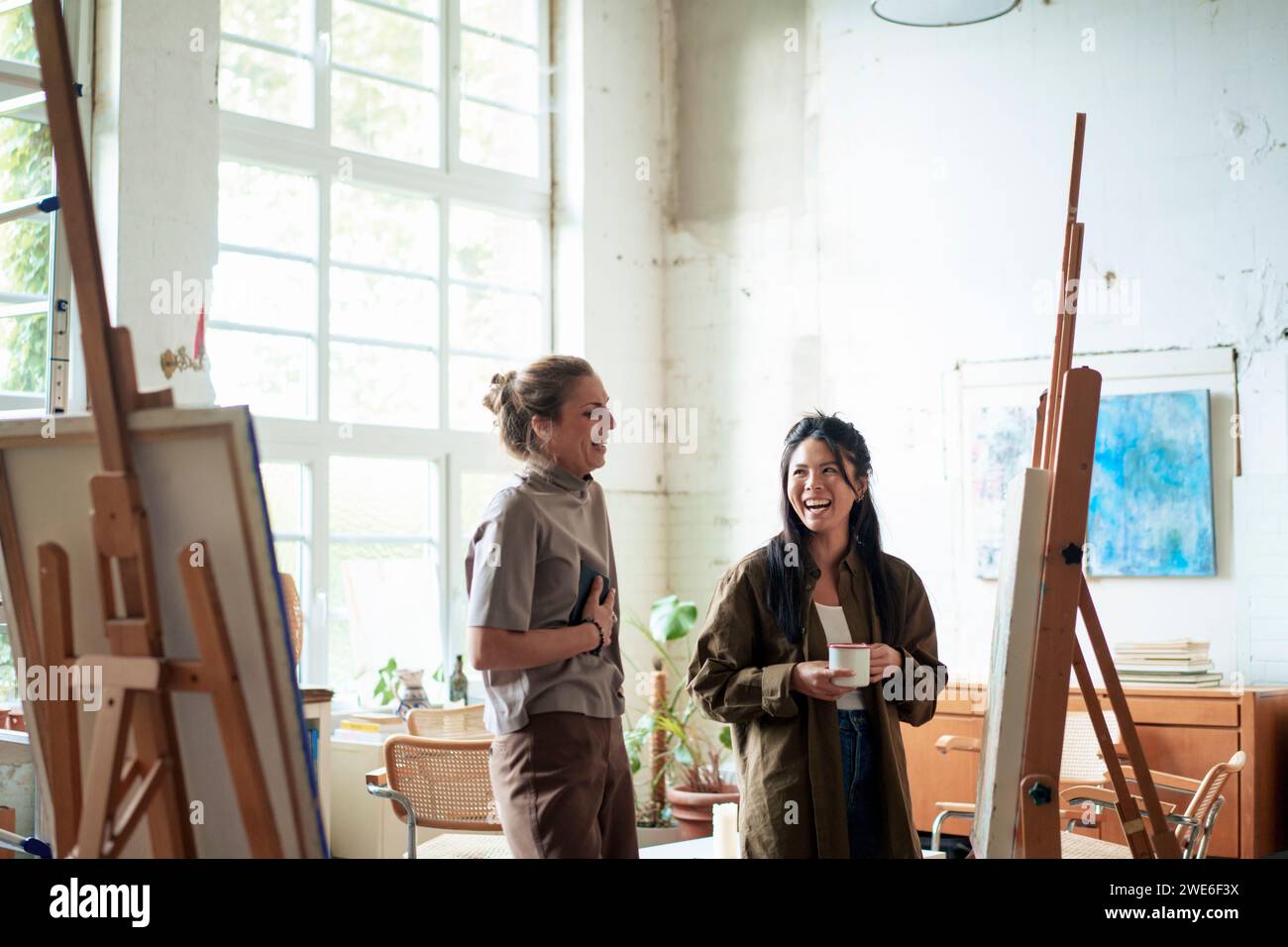 Happy women discussing over painting on easel in art studio Stock Photo ...