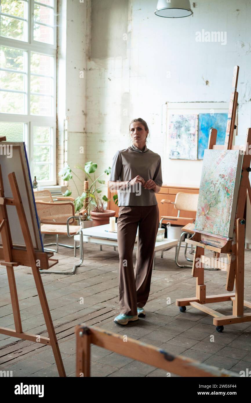 Confident painter standing by painting on easel in workshop Stock Photo ...
