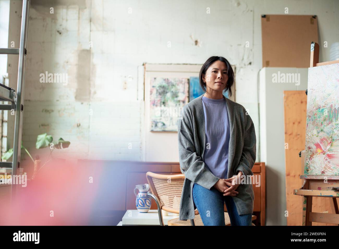 Confident painter standing by painting on easel in workshop Stock Photo ...